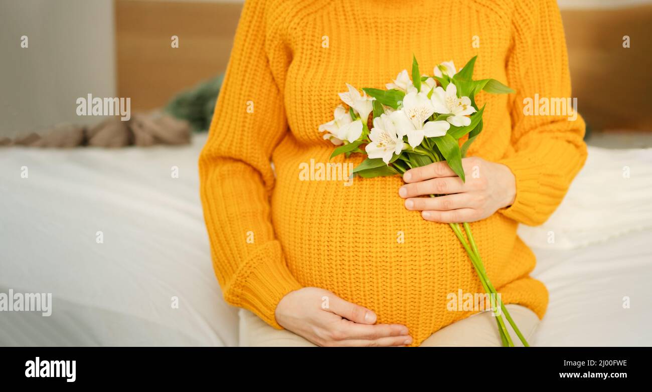 Beautiful pregnant woman with a bouquet of flowers in her hand strokes ...