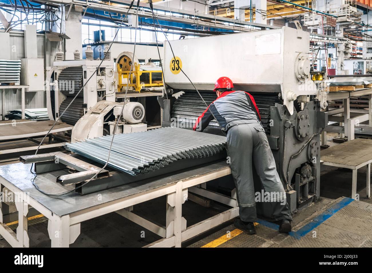 Factory worker with automatic metalforming machine and sheets of metal ...