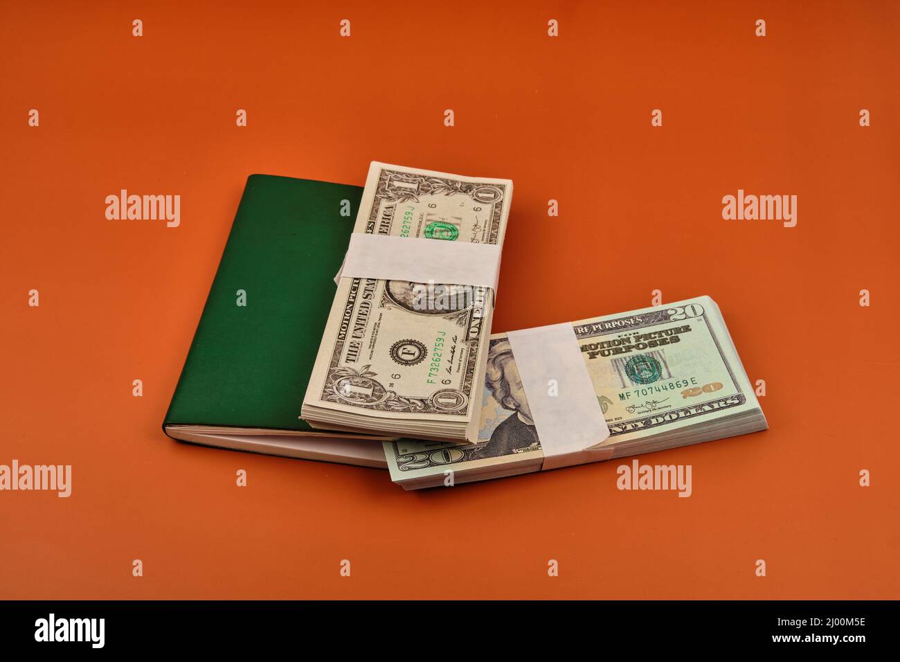 Green colored notebook with two bundles of dollars on an orange table ...