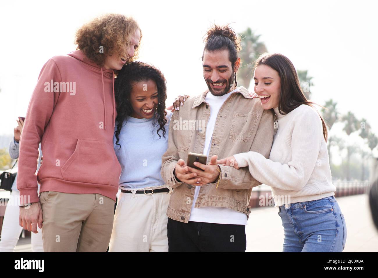 Group of happy friends using phone outdoors while walking al laughing ...