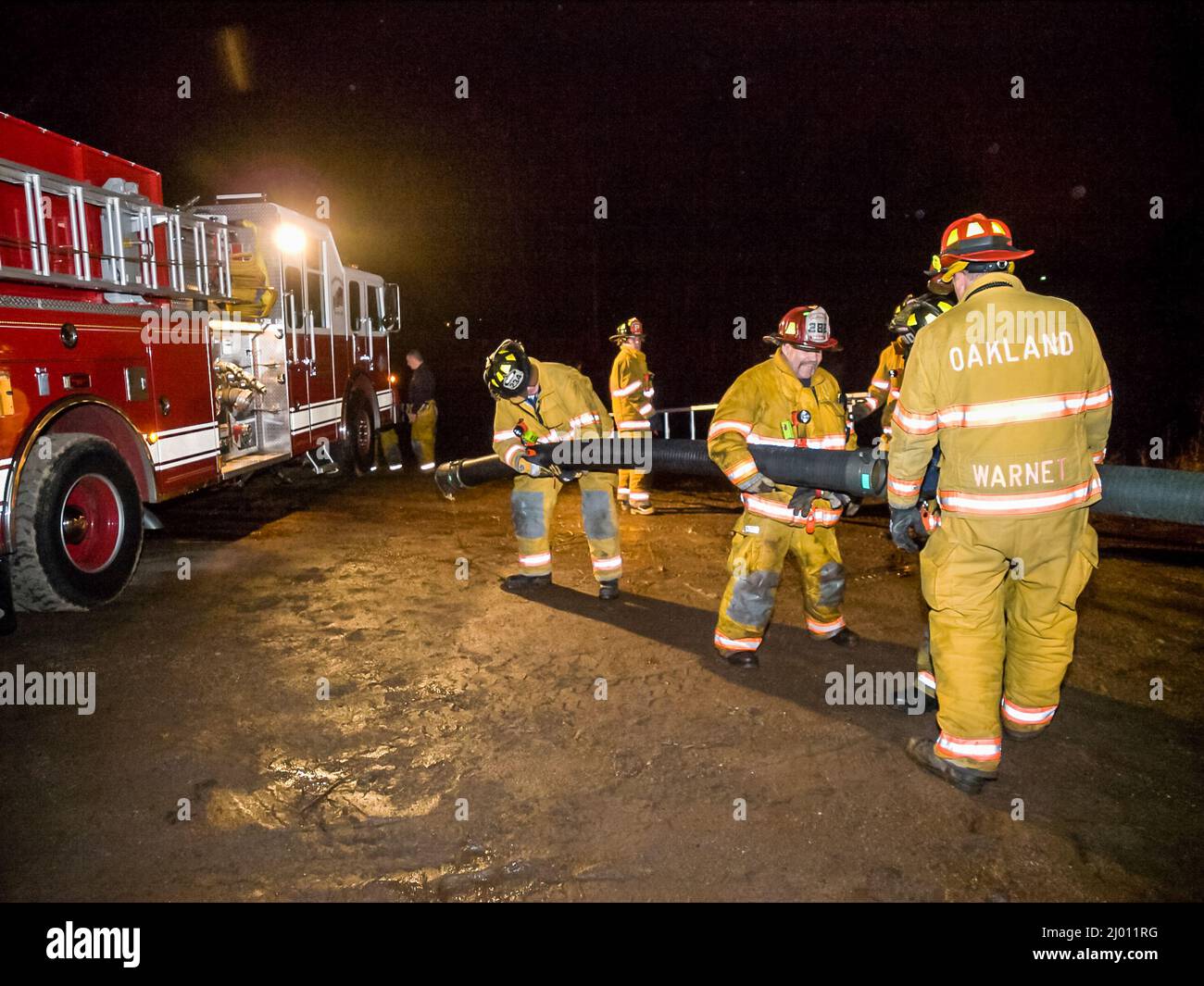 Firefighters in action at night with truck and hard suction hose Stock ...