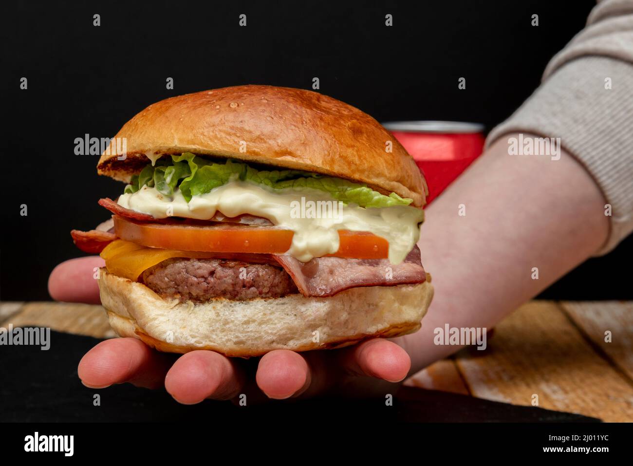 A hand holding a beef burger with cheddar cheese, tomato and bacon with ...