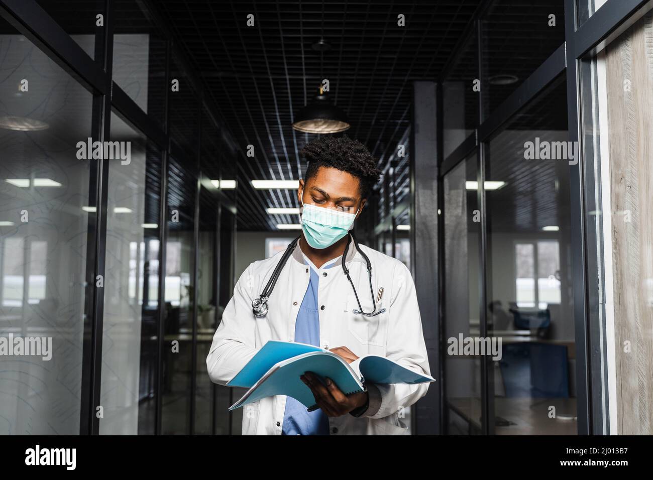 African doctor in mask with books in medical clinic. Black medical ...