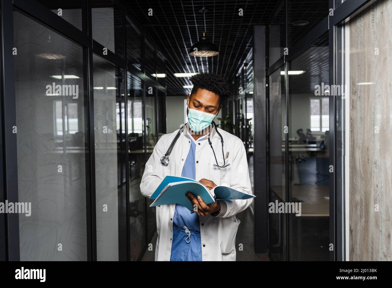 African doctor in mask with books in medical clinic. Black medical ...