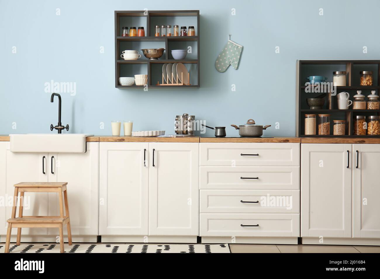 Interior of stylish kitchen with white counters, shelves and supplies ...