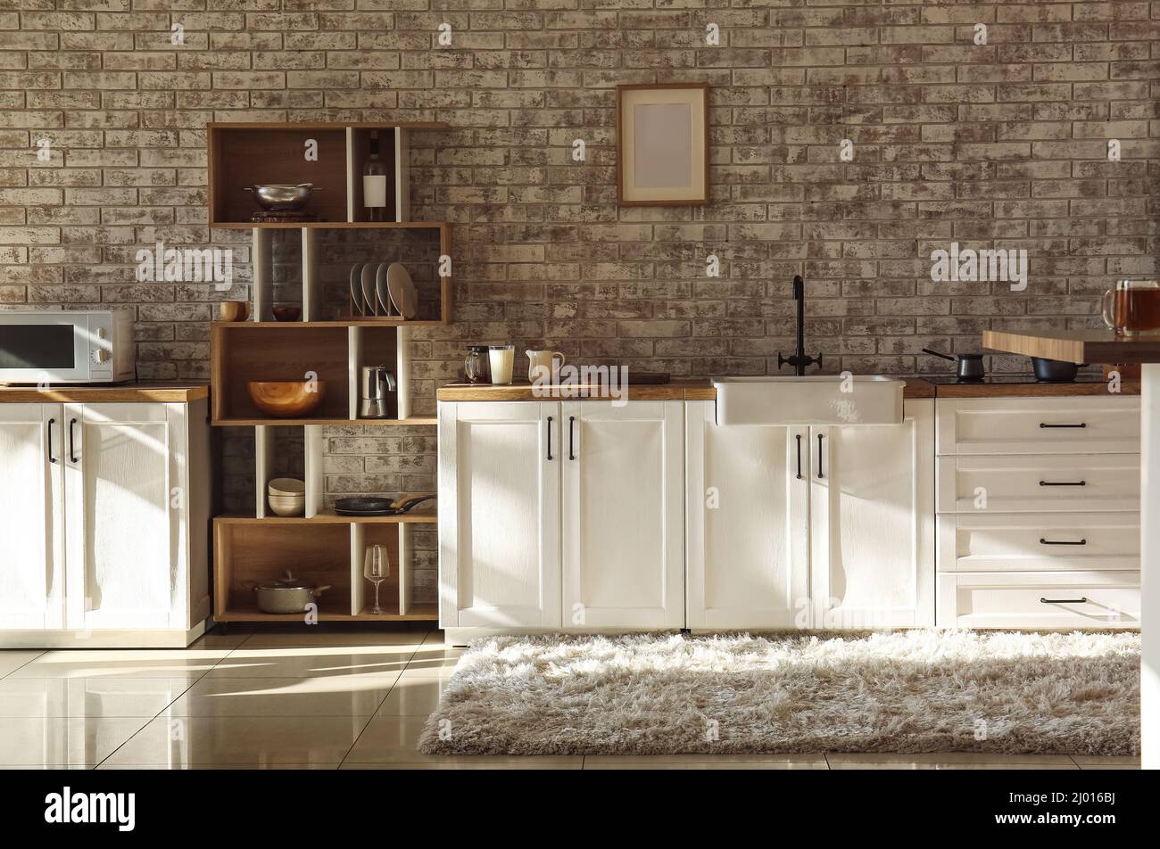 Interior of modern kitchen with white counters, shelving unit and brick ...