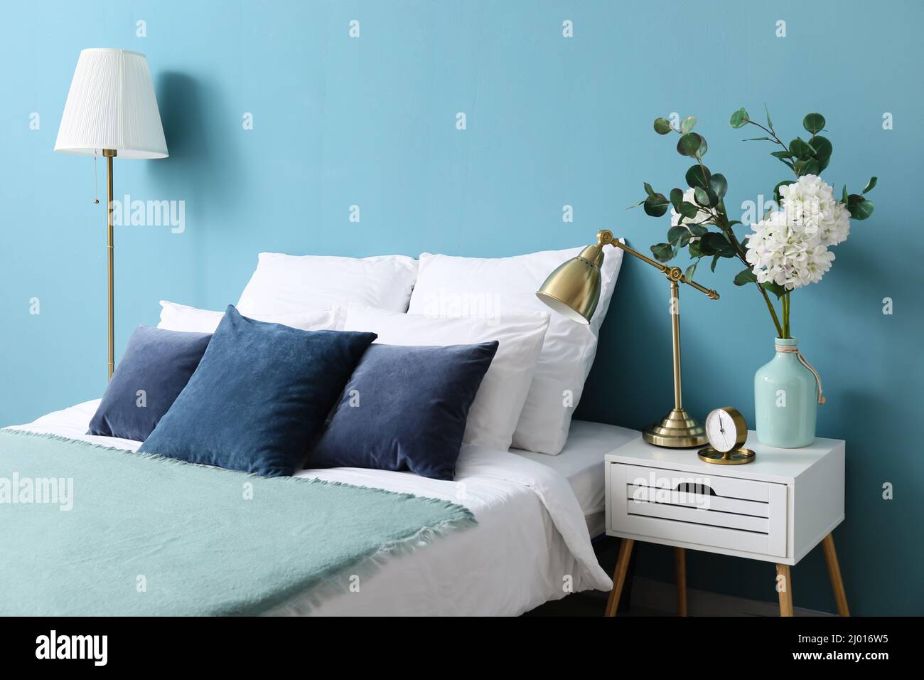 Comfortable bed, vase with flowers on nightstand table and modern lamp ...