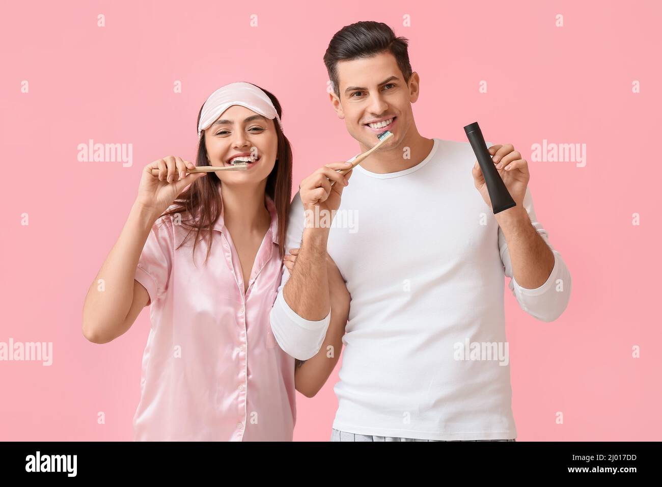 Young couple brushing teeth with activated charcoal tooth paste on pink ...