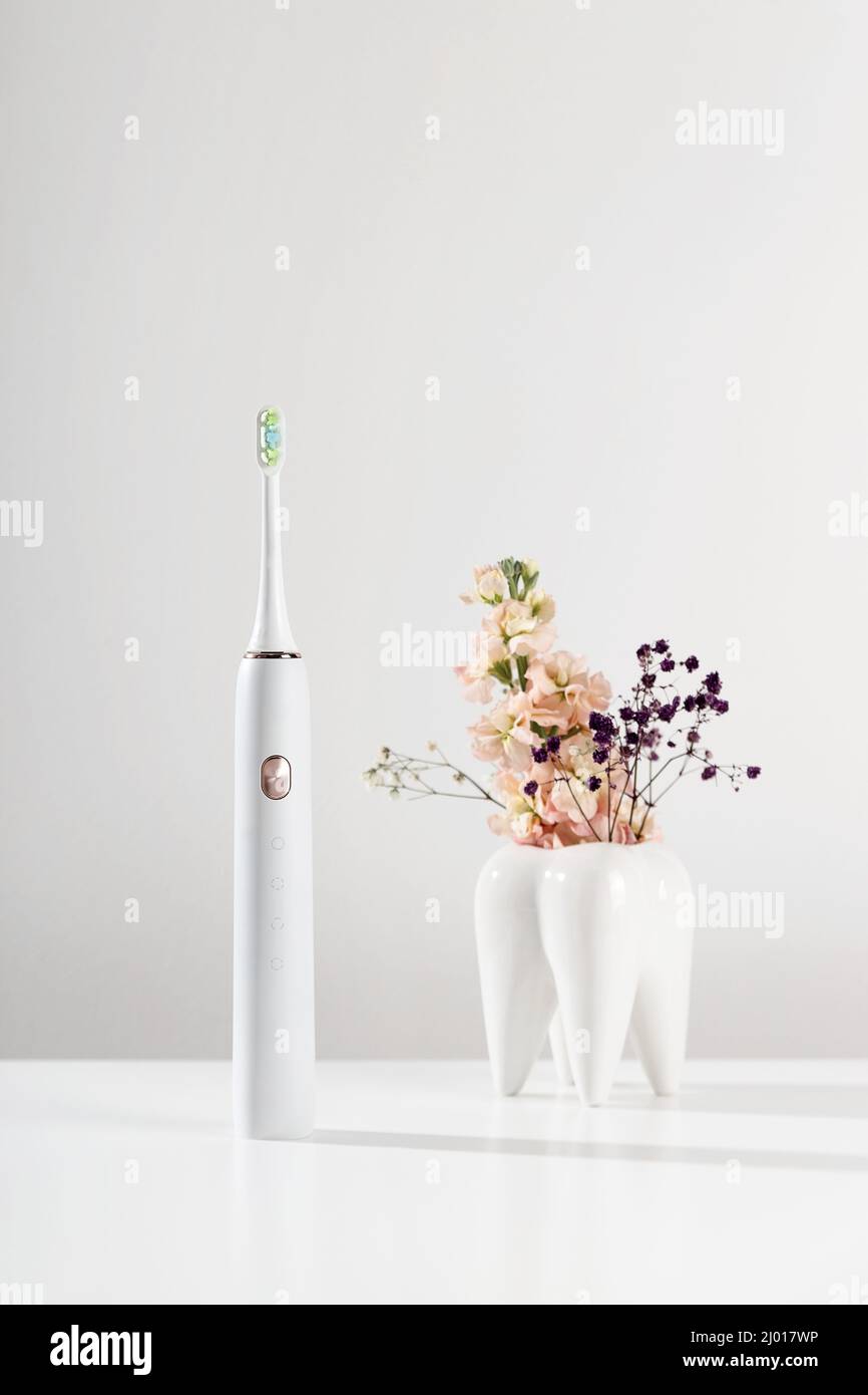 Electronic toothbrush next to decorative model of tooth on white ...