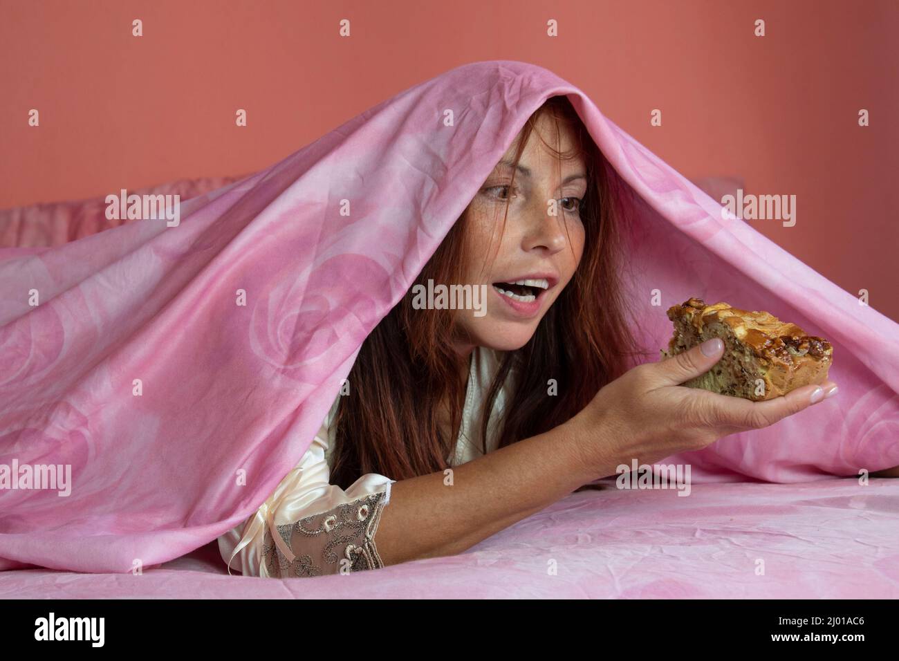 Night gluttony theme, woman on bed secretly eating a piece of pie Stock ...
