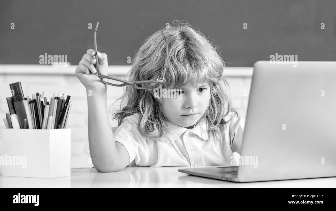 serious kid boy in glasses study online in school classrrom with laptop ...