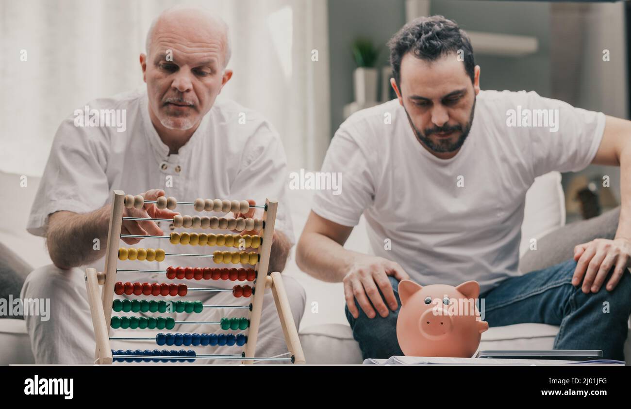 Senior man using an abacus to do financial calculations as his son sirs ...