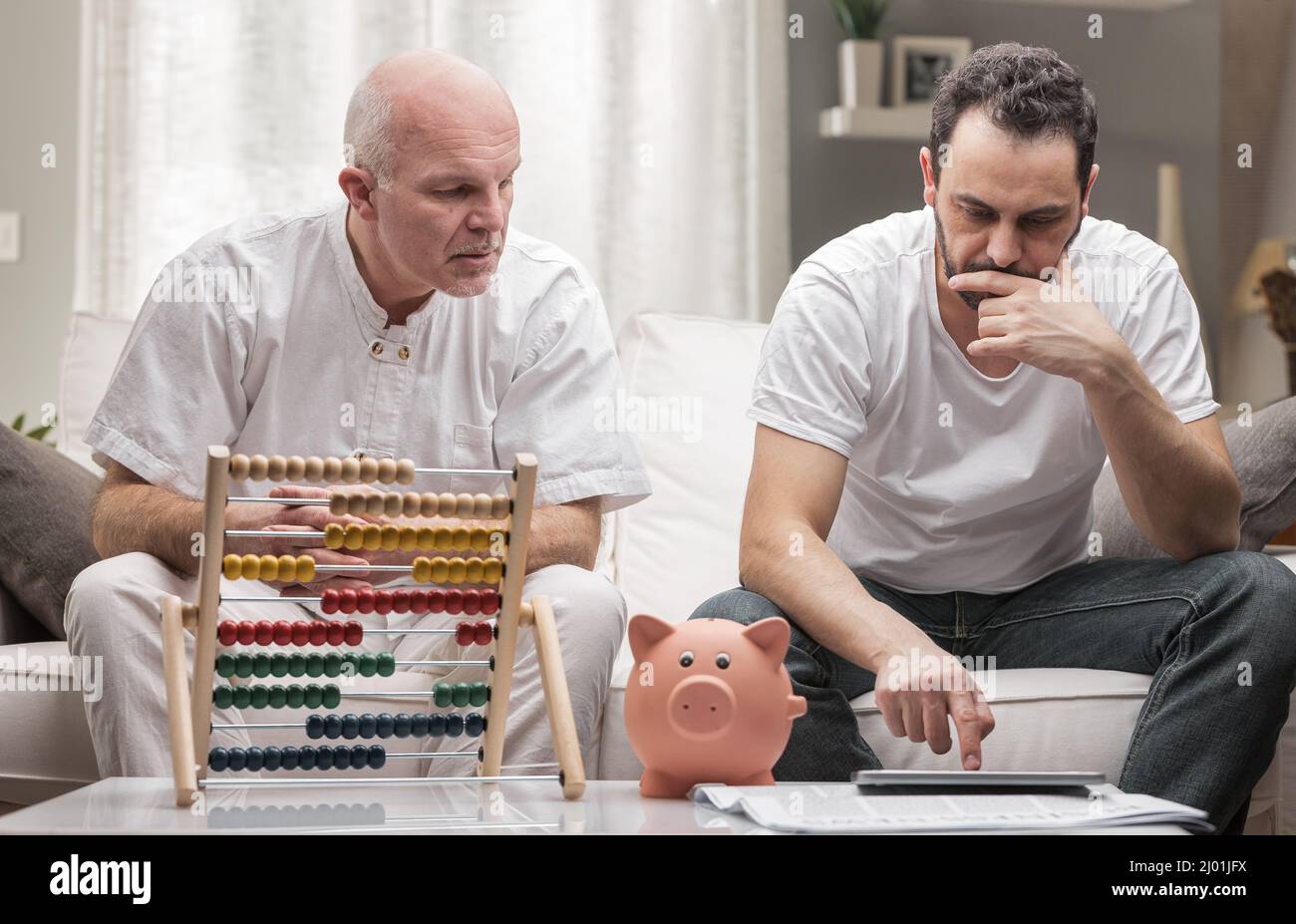 Two generations of men sitting doing financial calculations, the senior ...