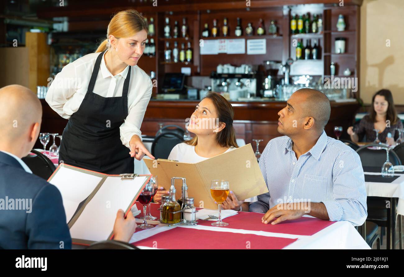 Restaurant guests will choose dish from the menu. Polite waitress helps ...