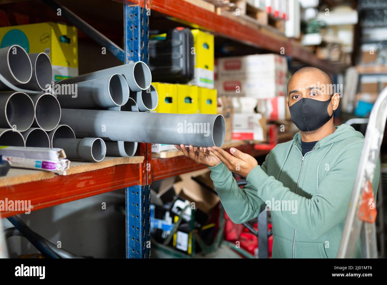 Craftsman in protective mask selects plastic plumbing pipes in hardware ...