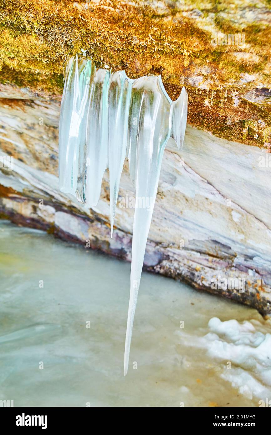 Smooth and sharp icicle formation attached to mossy rocks Stock Photo ...