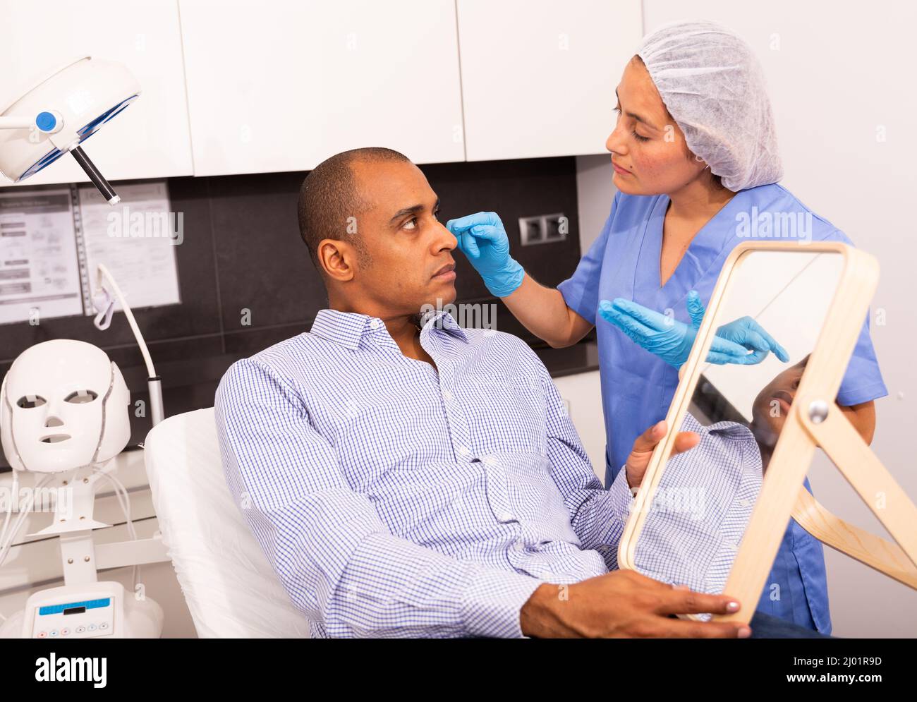 Cosmetologist examining male client face before procedure Stock Photo ...