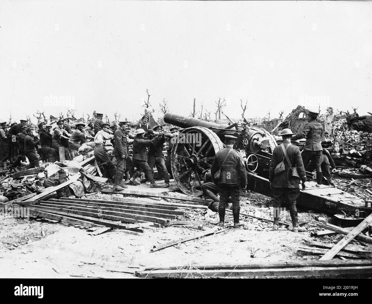 A large group of soldiers attempting to pull a field gun on to a wooden ...