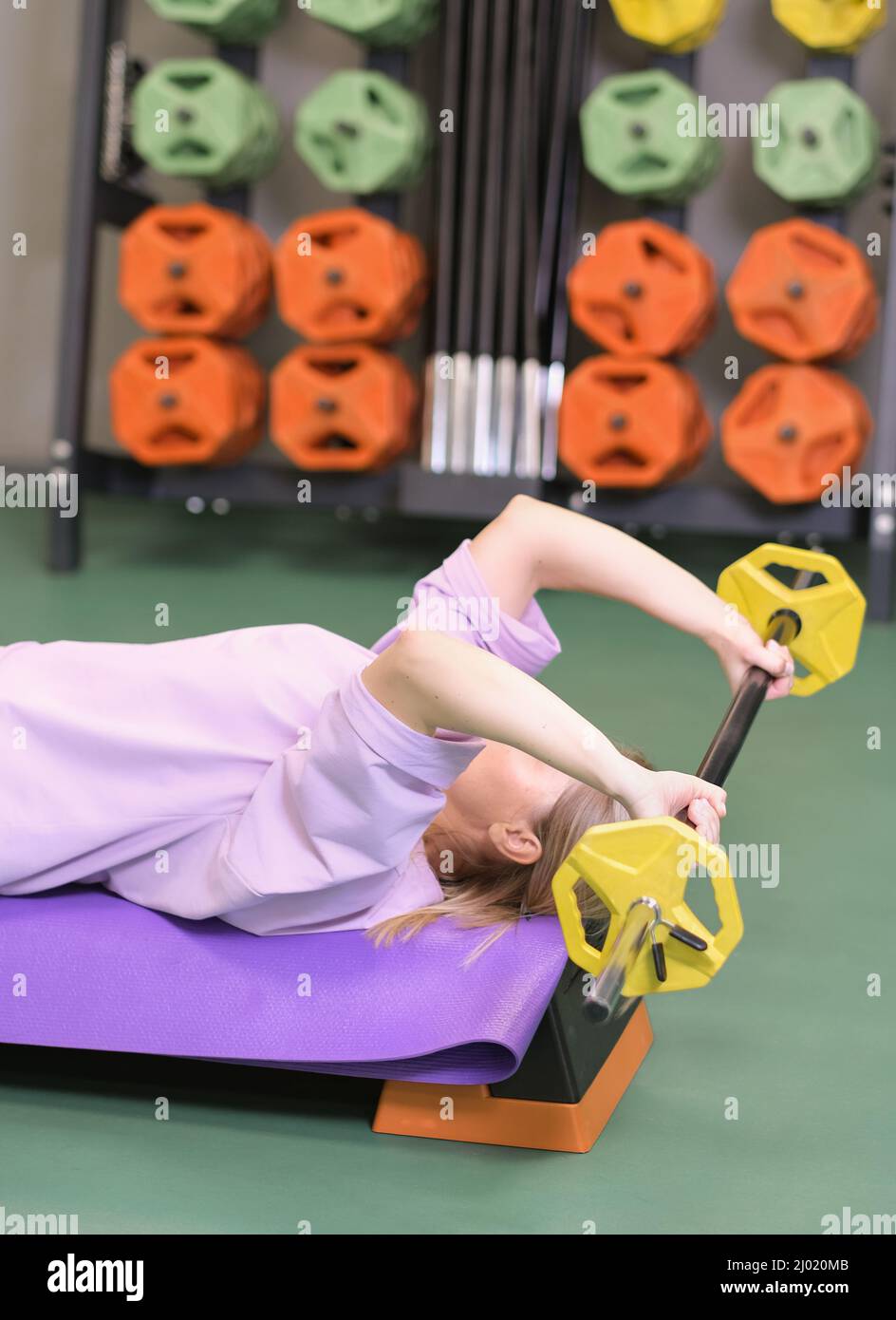 woman lying on training bench lifting barbell in gym, pushing exercise ...