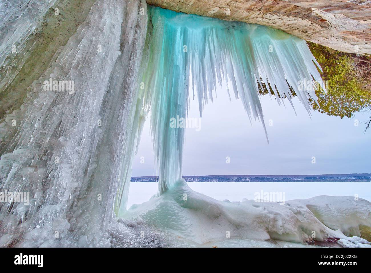 Large sharp blue icicles hanging from rocks next to frozen lake in ... Large sharp blue icicles hanging from rocks next to frozen lake in ...