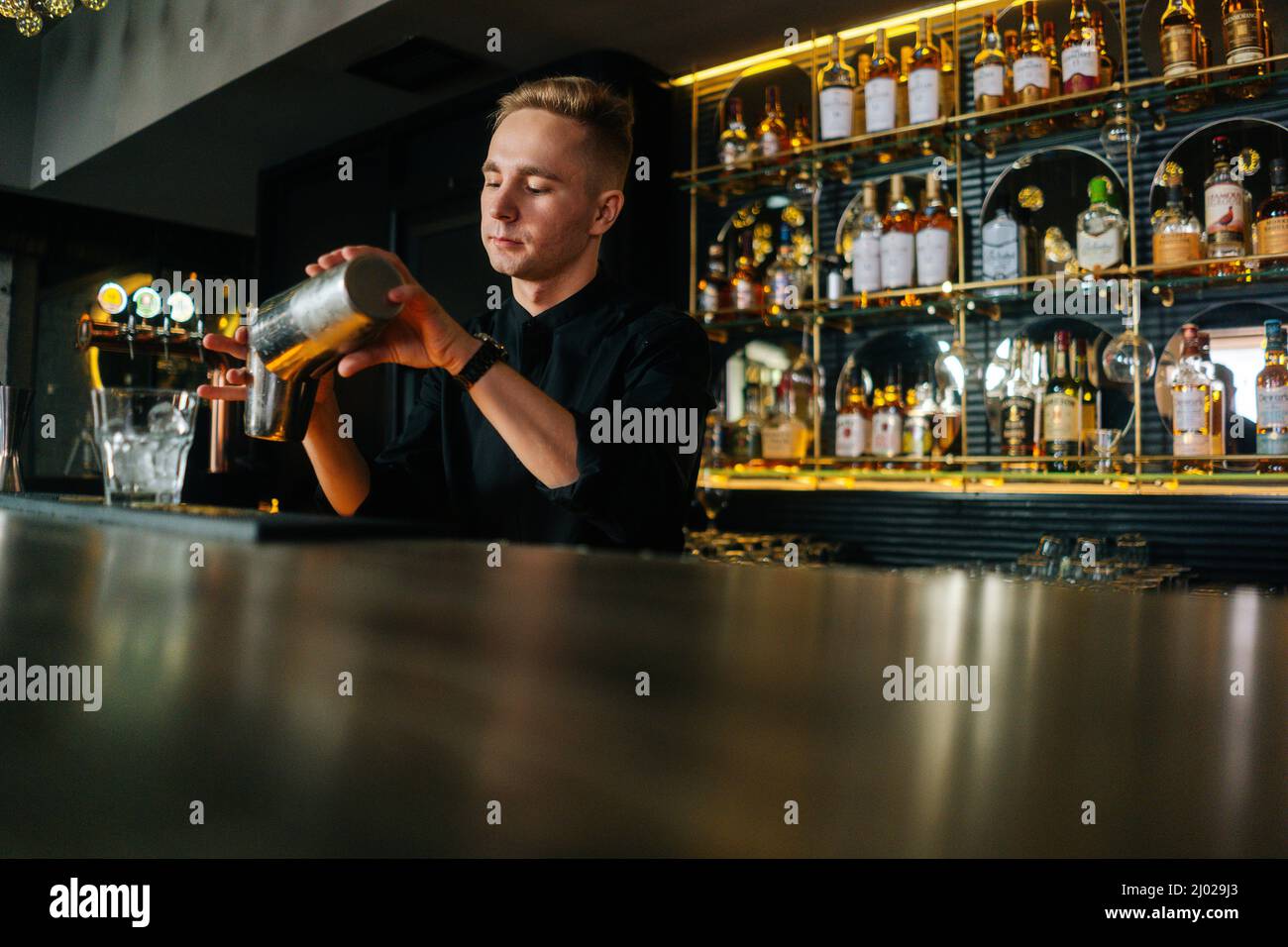 Low-angle view of handsome bartender preparing refreshing alcoholic ...