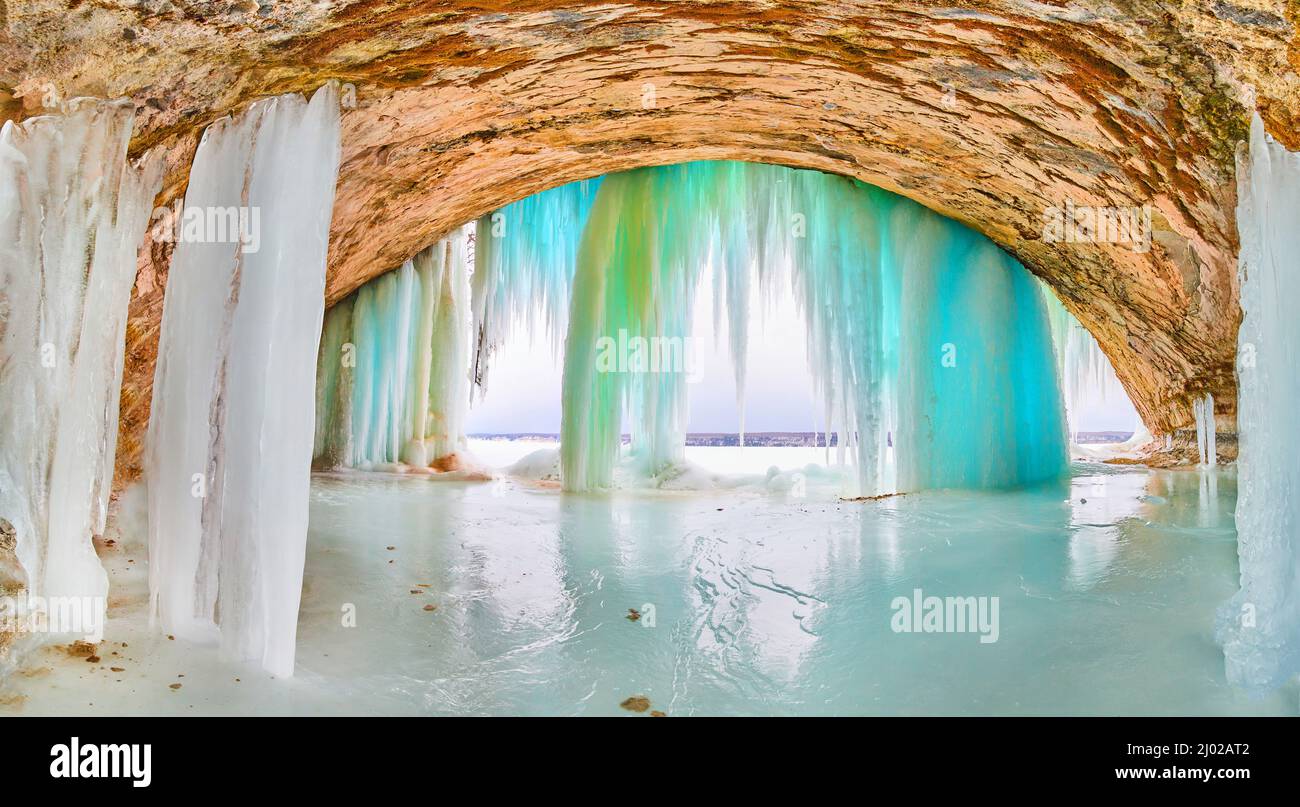 Giant ice cave with tall icicles of blue and green at entrance on lake ...