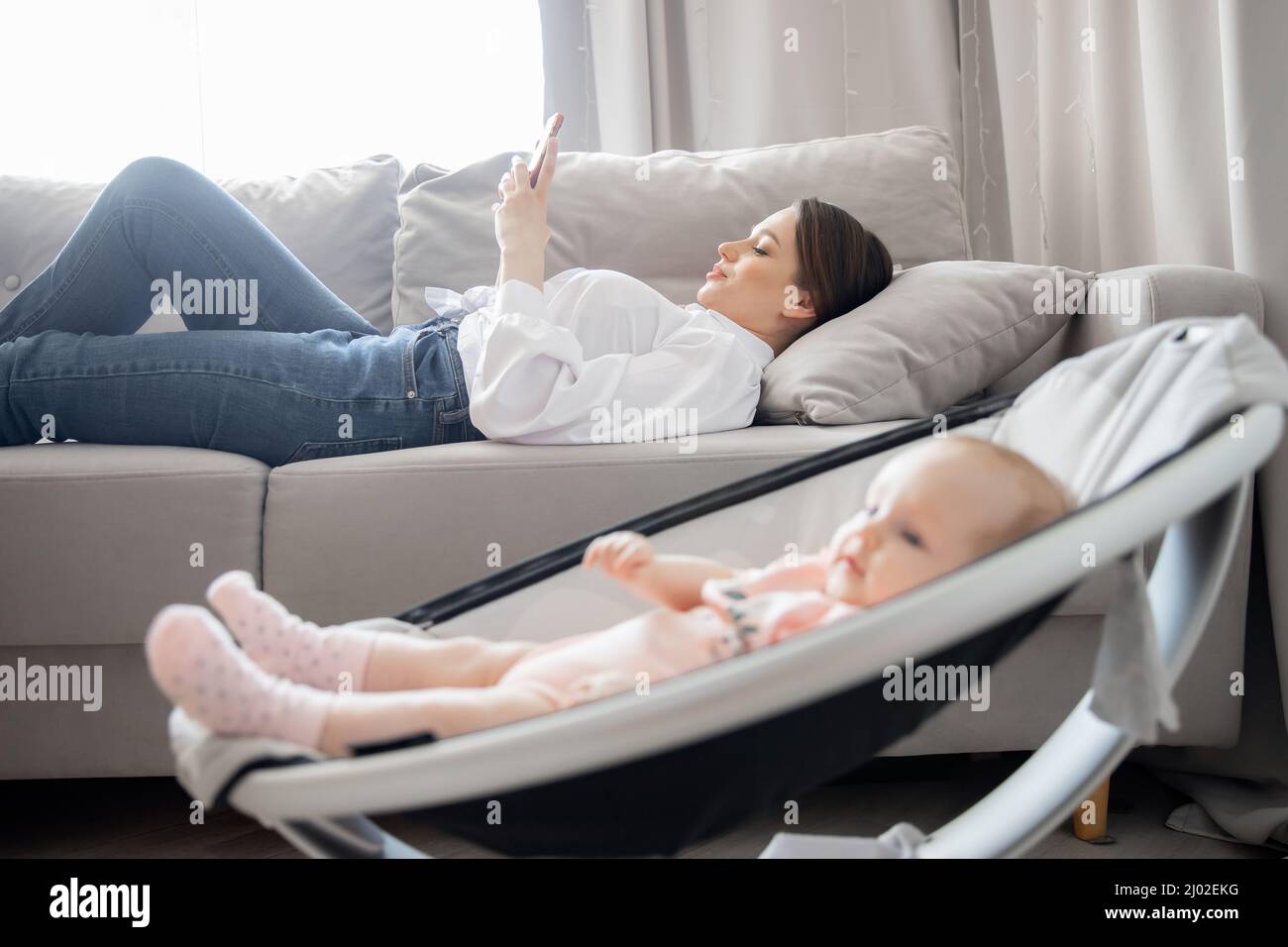 Young woman mom works internet with phone while baby sleeps in ...