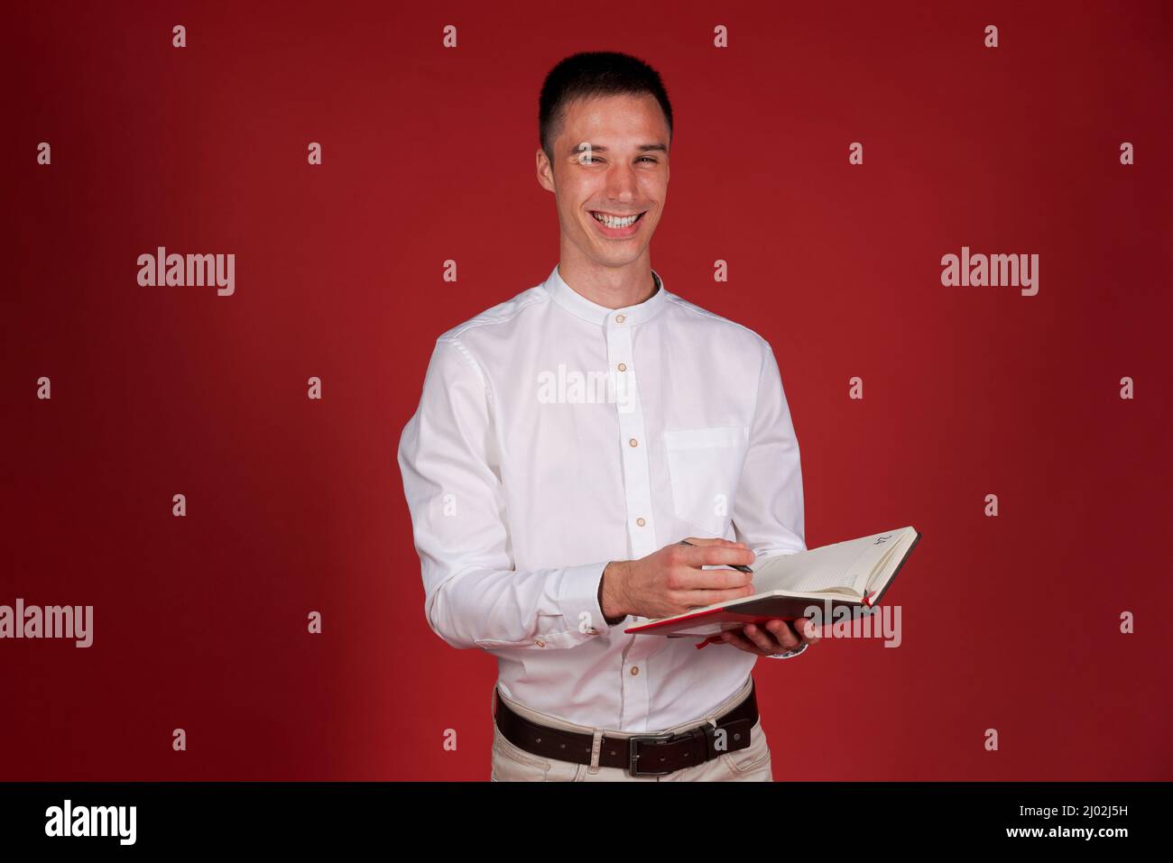 Happy businessman smiling and writing in notepad with pen while wearing ...