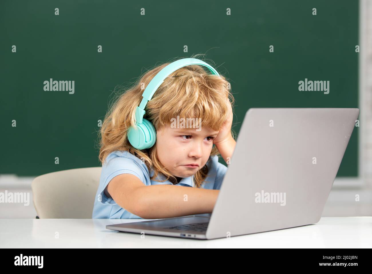 Angry sad child boy in headphones using a laptop and study online with ...