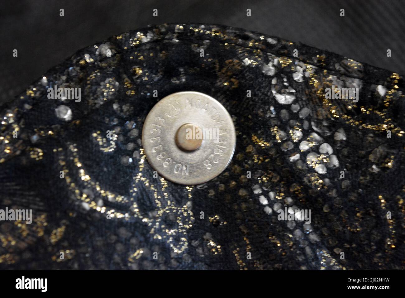 The round metal magnetic button is sewn into a black dark fabric with ...