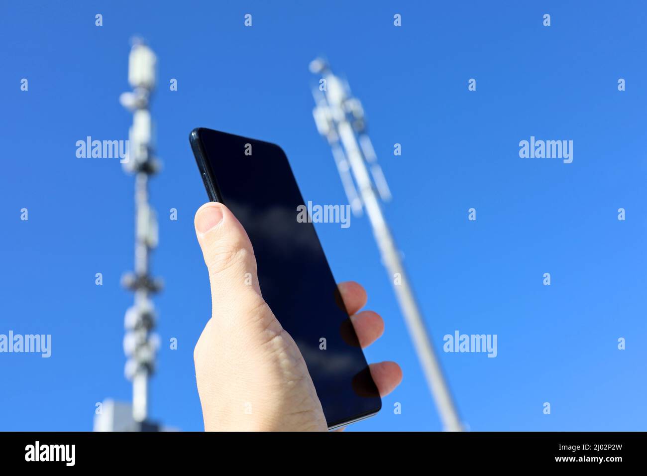 Smartphone in hand on background of cell towers. Mobile telecommunication equipment, phone ...