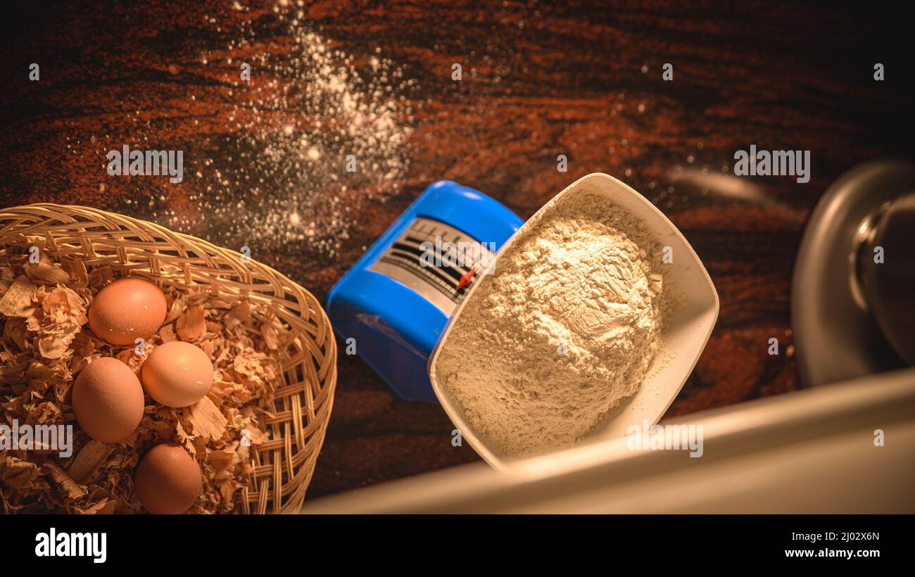 Top view of flour on the scale and eggs in a straw basket on a table in ...