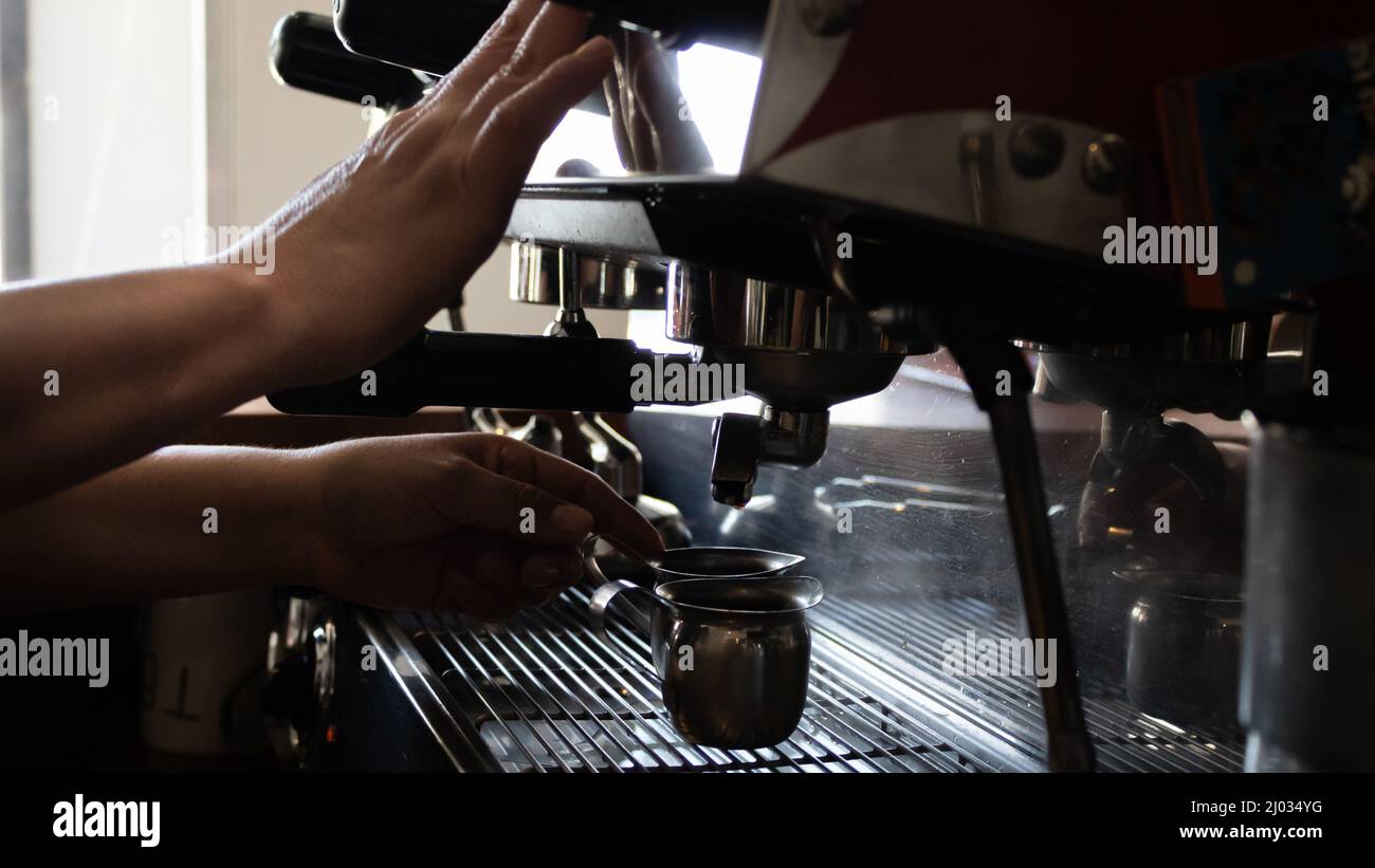 hands of a young woman pouring coffee into two cups in a machine inside ...