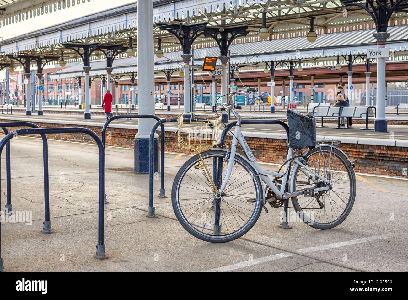 A bicycle with a basket parked on a railway station platform. Other ...