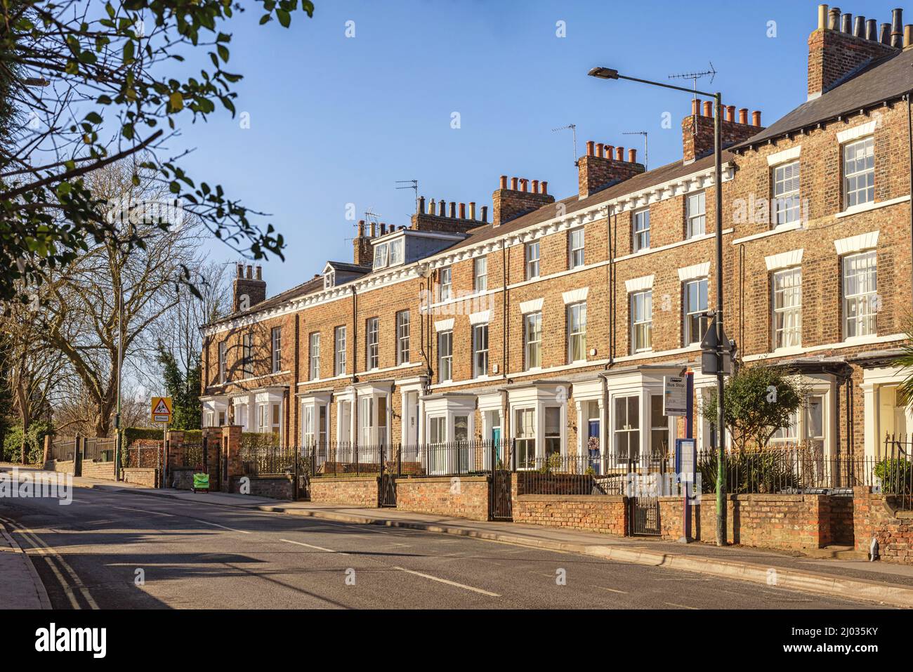 A street of terraced houses on a gentle upward slope. Shadows fall onto ...