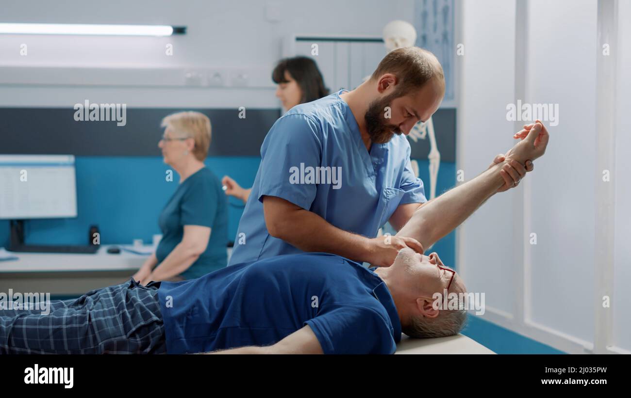 Physiotherapist assisting elder patient to stretch arms muscles, giving ...