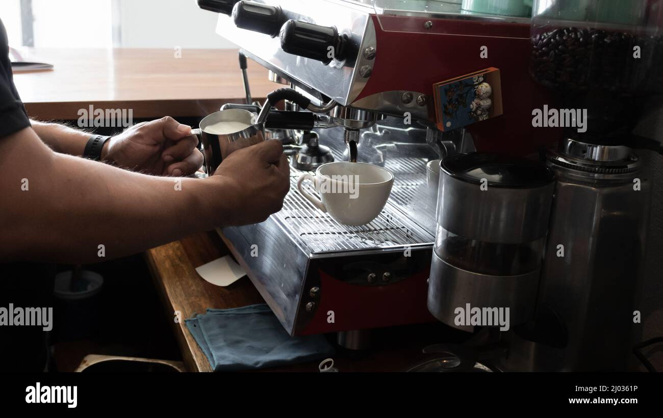 young adult employee heating milk to make coffee in a coffee shop in ... young adult employee heating milk to make coffee in a coffee shop in ...