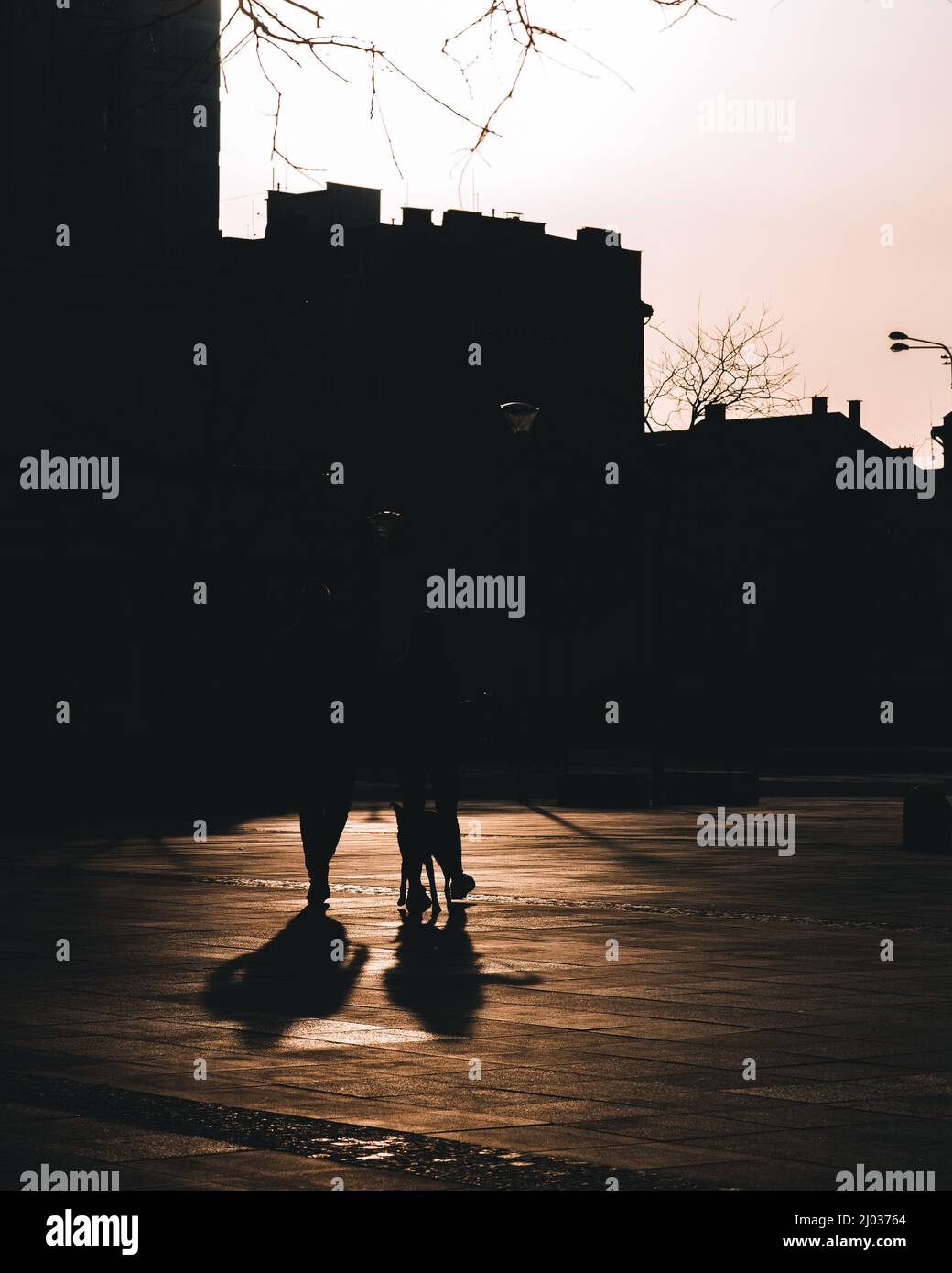 Two people walking at the sunset in the shadows with the building in ...