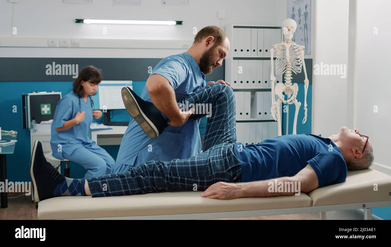 Medical assistant supporting old man in doing physical exercise to ...