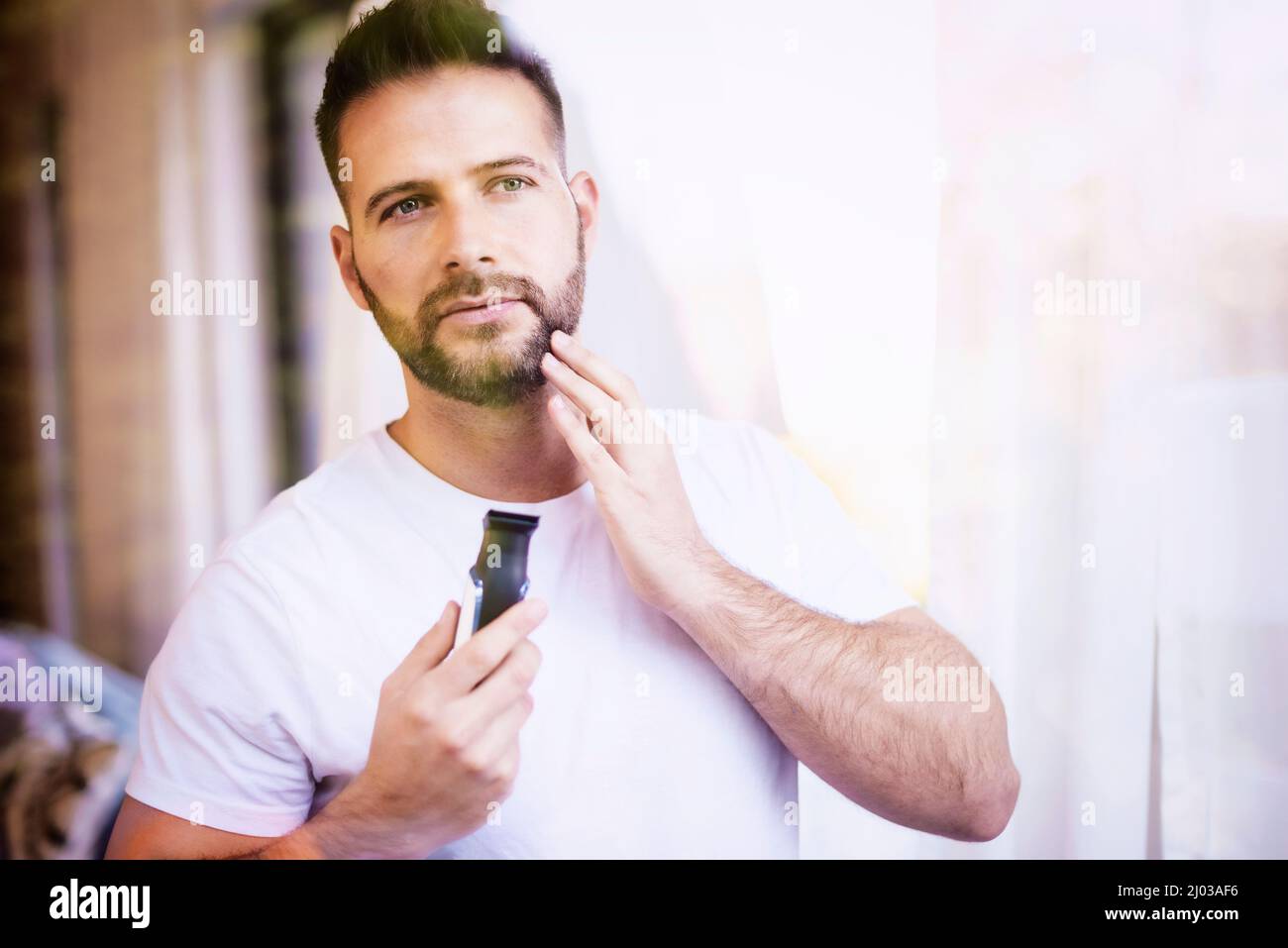 Portrait of a young man shaving his face with an electric razor at home ...