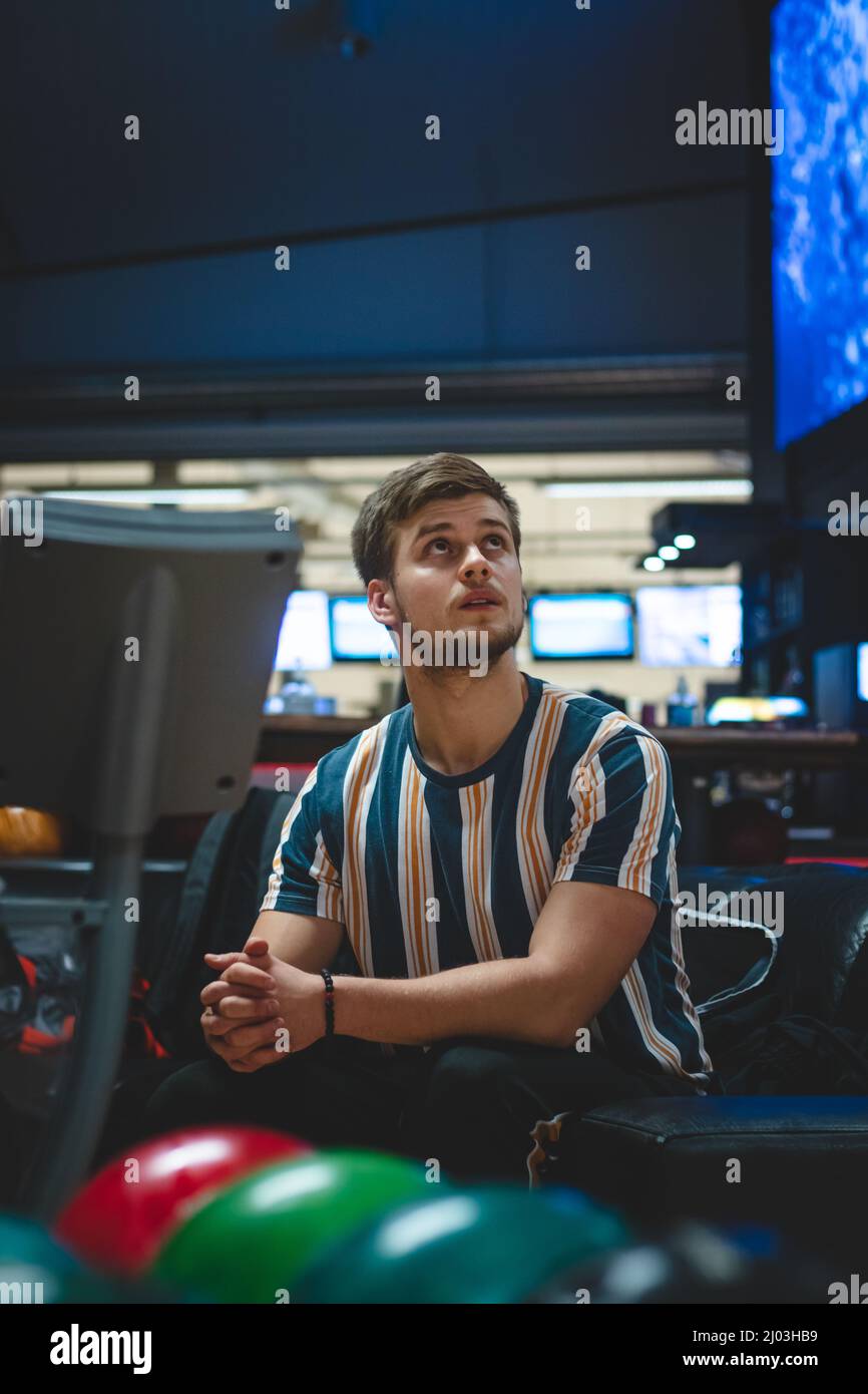 Focused professional bowling guy sits on the bench and watches the ...