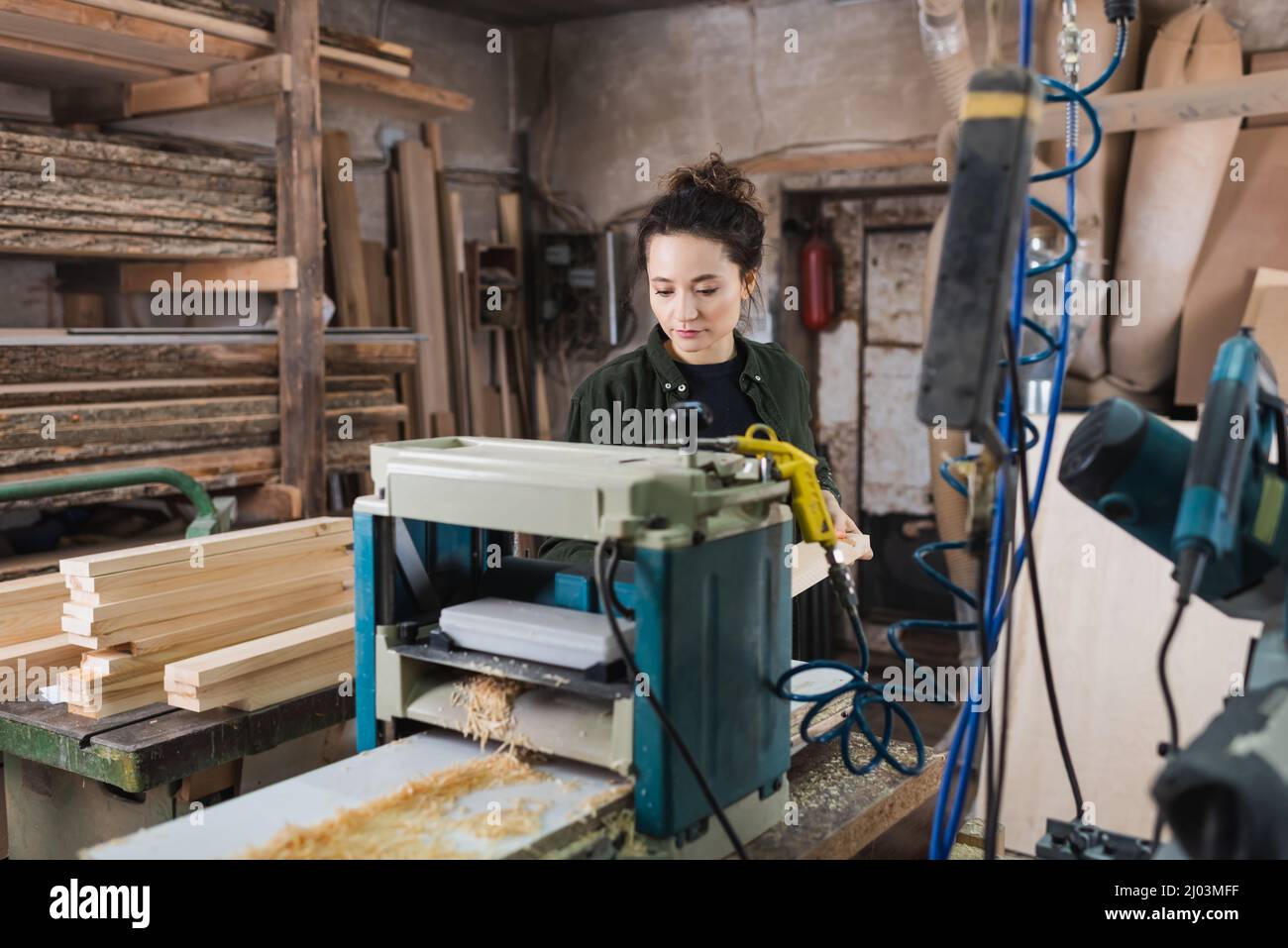 Young carpenter standing near bench thicknesser and wooden planks in ...