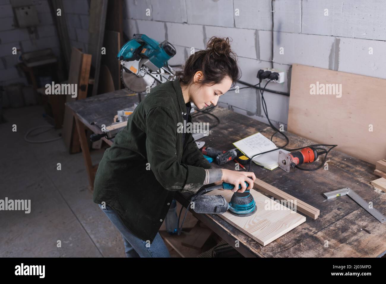 Side view of woodworker sanding board near tools and miter saw in ...