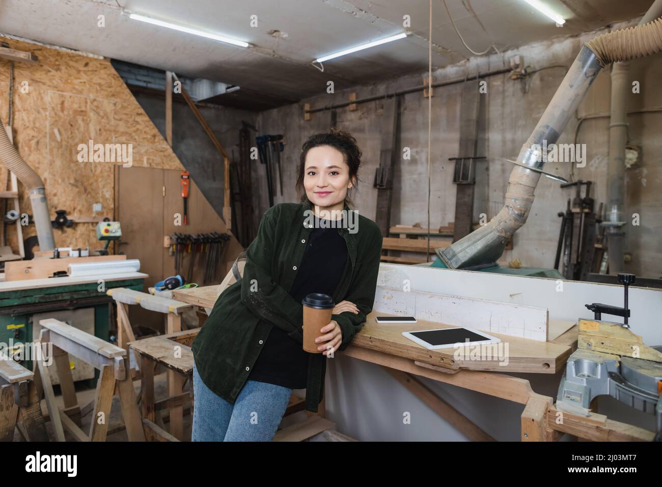 Cheerful carpenter holding coffee to go and looking at camera in ...