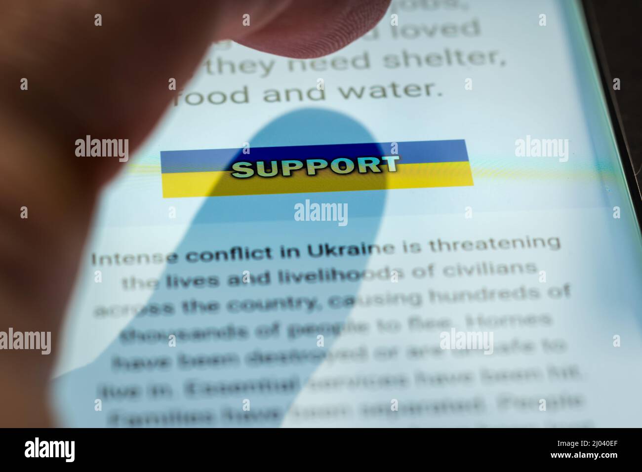 Close-up finger pressing support button over ukraine flag on smartphone ...