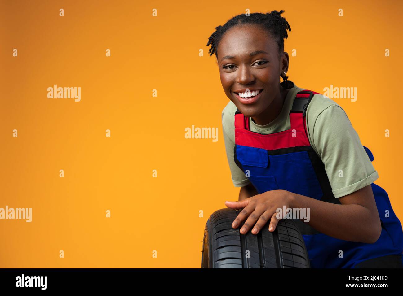 Portrait of smiling black female mechanic posing with new car tyres in ...