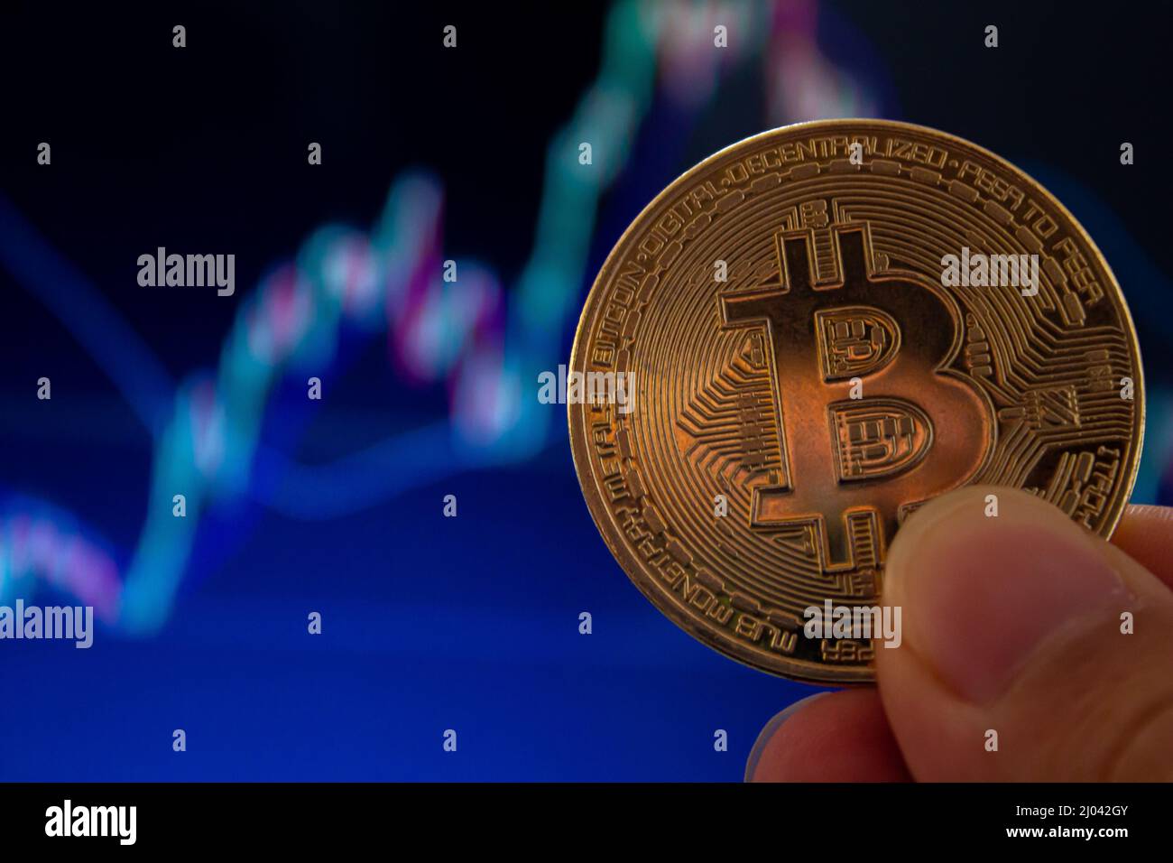Hand holding bitcoin, blurred stock market chart in the background ...
