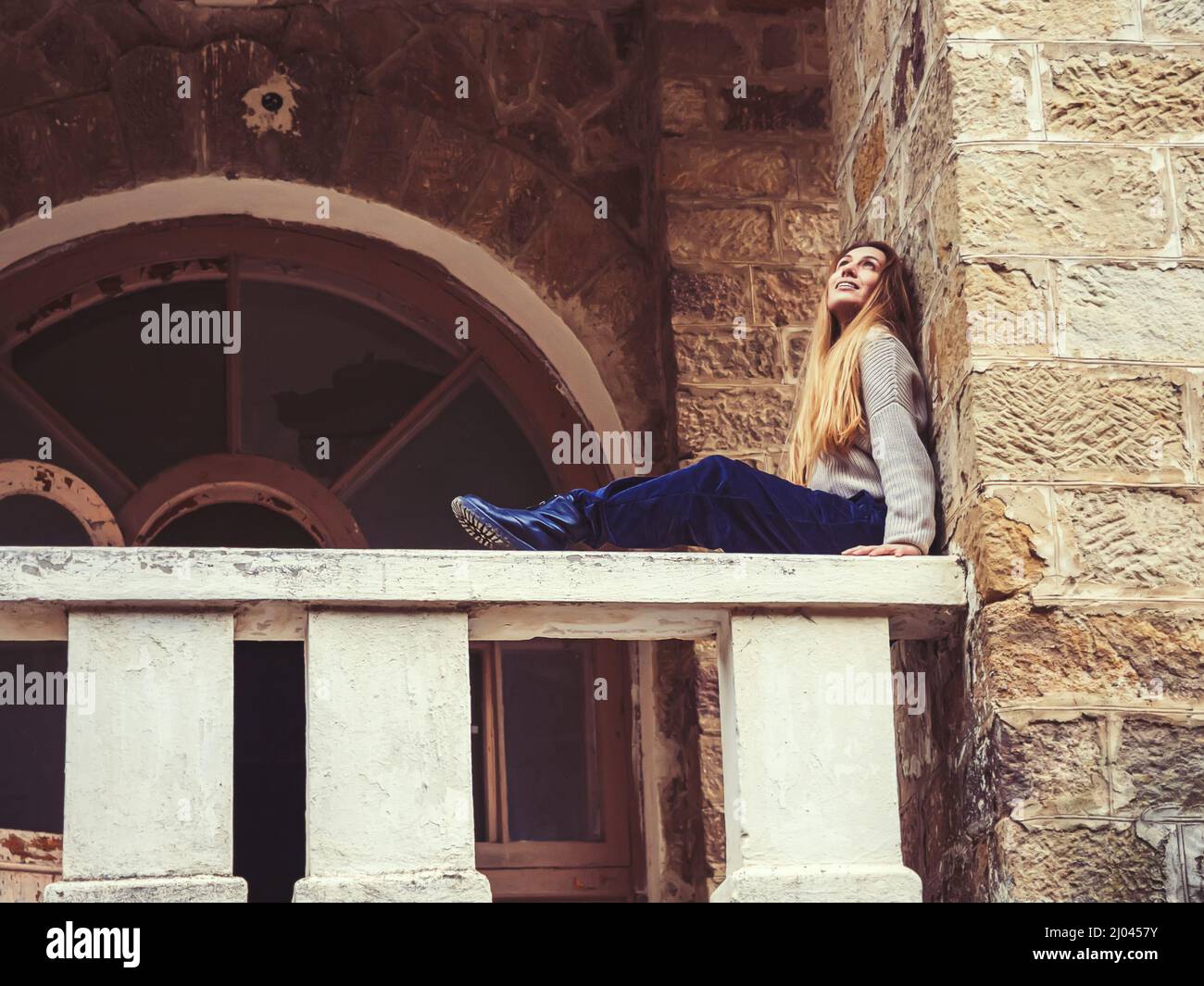 Dreamy woman sitting on the railing of veranda of an old abandoned ...