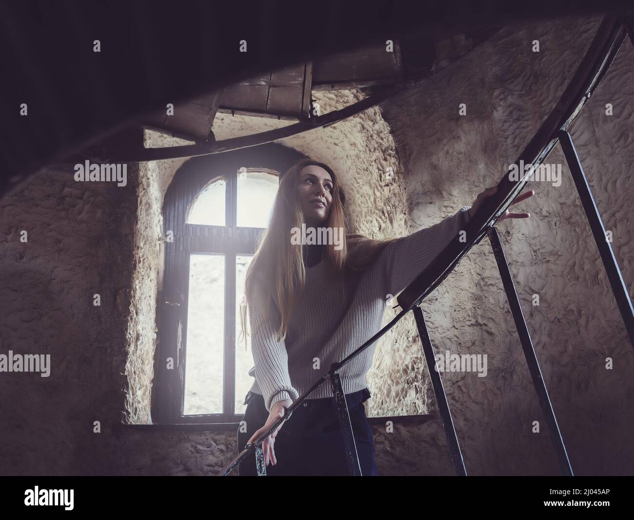 A woman stands holding on to the railing on the spiral staircase of the ...