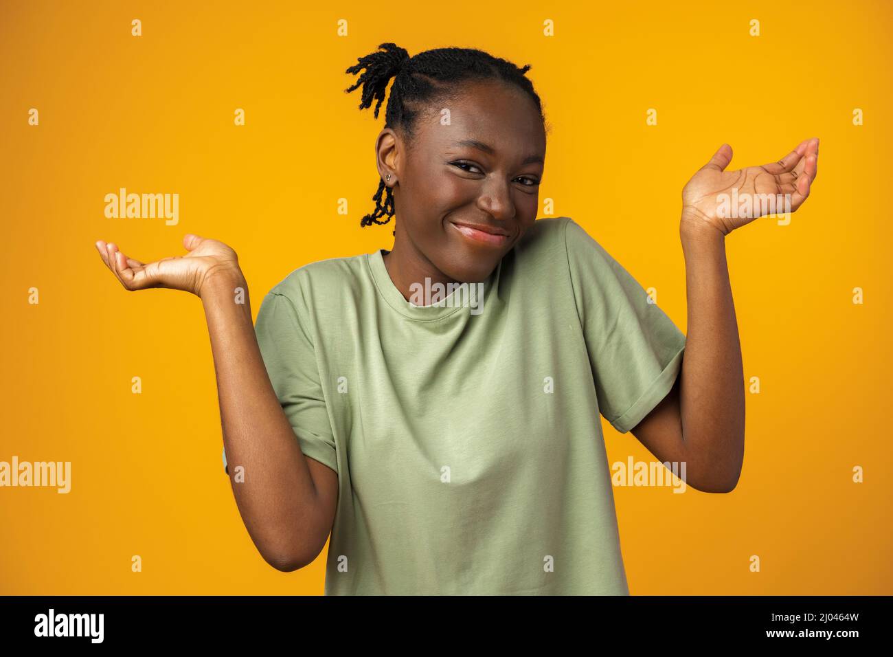 Puzzled and clueless young African woman with arms out in yellow studio ...